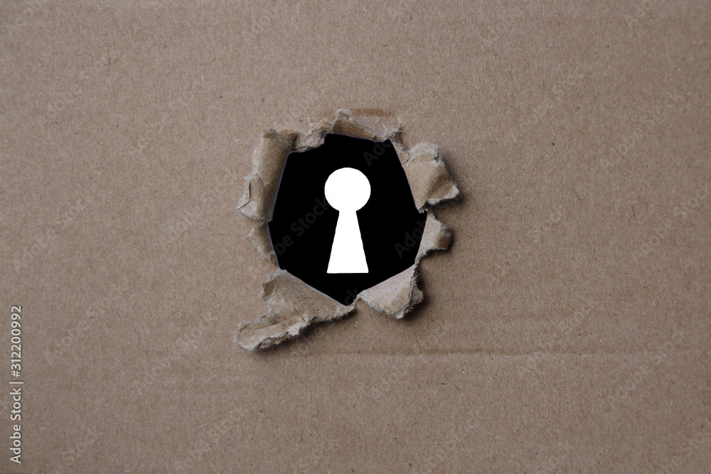 black keyhole in a torn hole of gray rough cardboard as a symbol of ...
