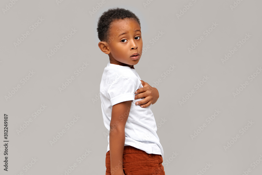 Isolated portrait of perplexed dark-skinned boy dressed in white t ...
