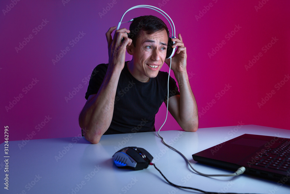 Angry gamer wearing headphones playing video games on computer in a ...