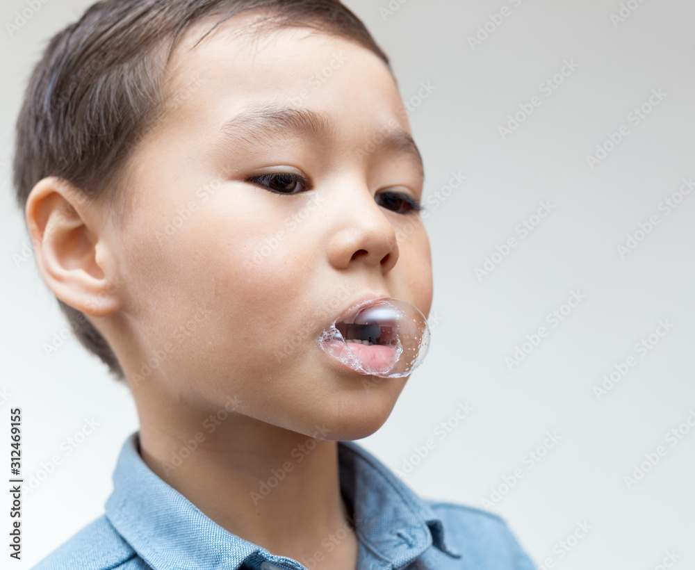 little boy tries to release bubbles of saliva from the mouth on a white ...