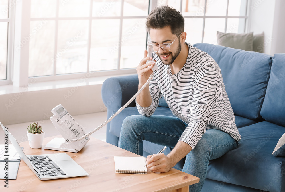 Young man talking by telephone and writing in notebook at home Stock ...