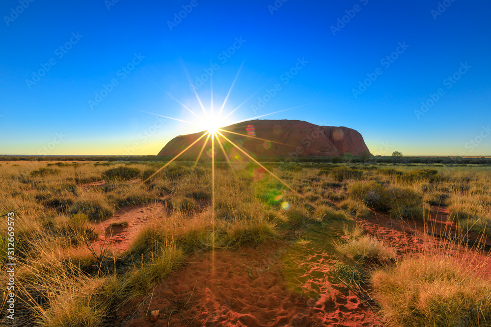 Dramatic sunbeams behind the huge Ayers Rock at down monolith. Colors ...