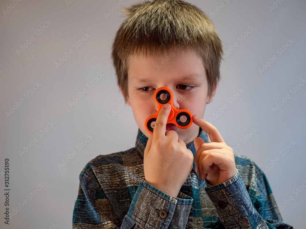 Funny blond child in colored shirt twists spinner on his nose. Portrait ...