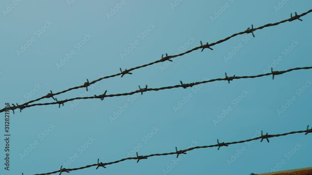 Twisted barb wires between metal poles placed on top of a metal fence ...