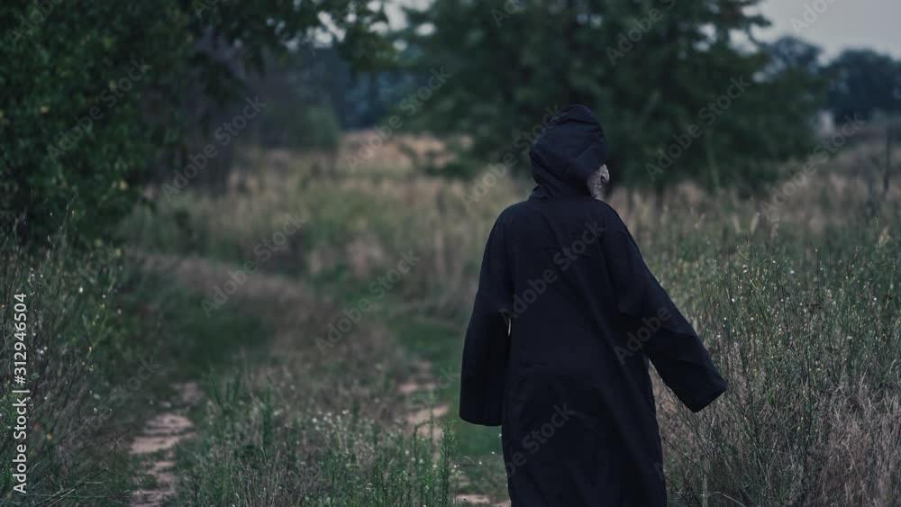 Backside portrait of death in nature. Dark figure in black costume out ...