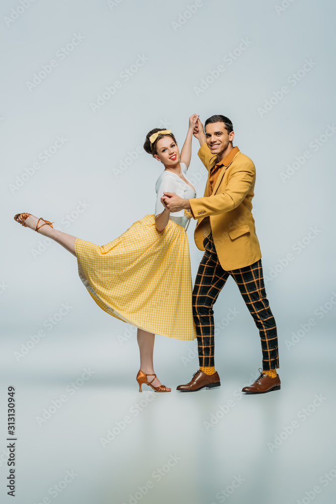 stylish dancers holding hands while dancing boogie-woogie on grey ...
