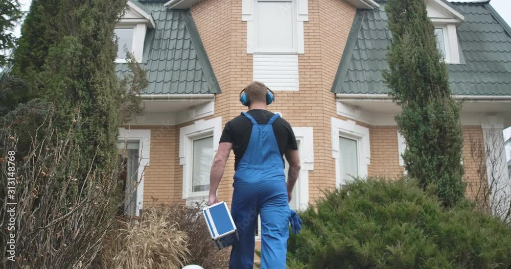 Back view of young Caucasian man in earphones and blue workrobe coming ...