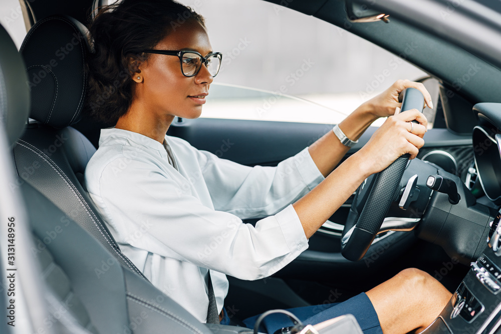 Woman driving a car. Side view of a female driver wearing glasses and ...
