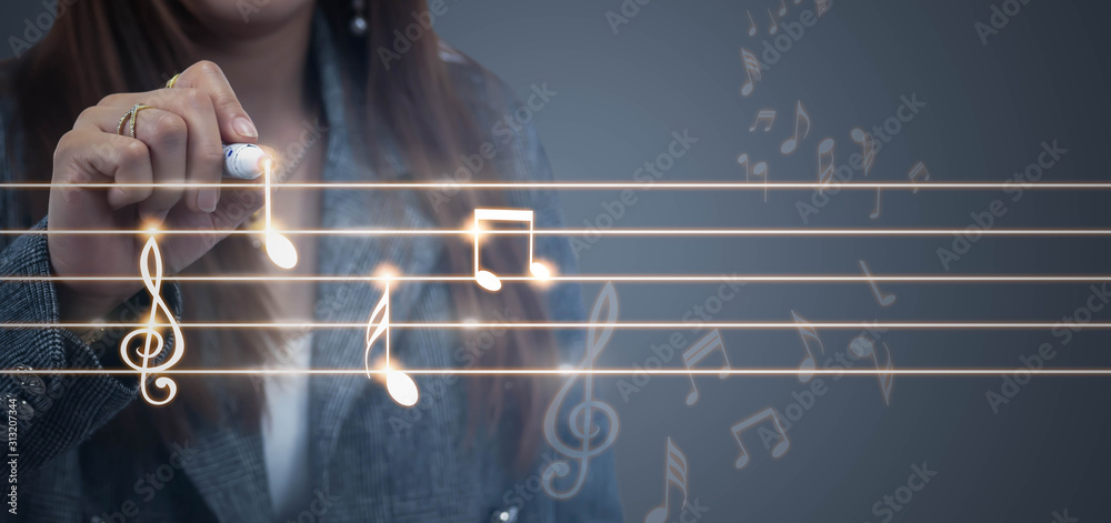 The women hands writing music notes on the glass in a room with a dark ...