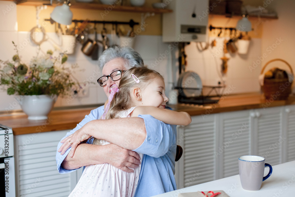 Grandmother hugging child in cozy kitchen at home. Happy family giving ...