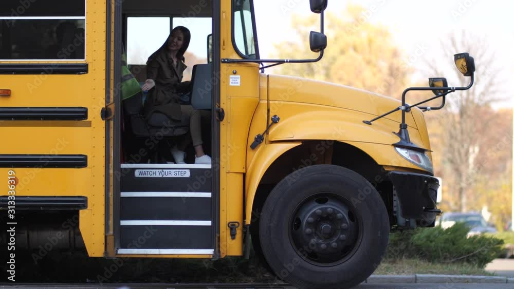 Friendly asian woman driver waving goodbye to elementary age pupils ...