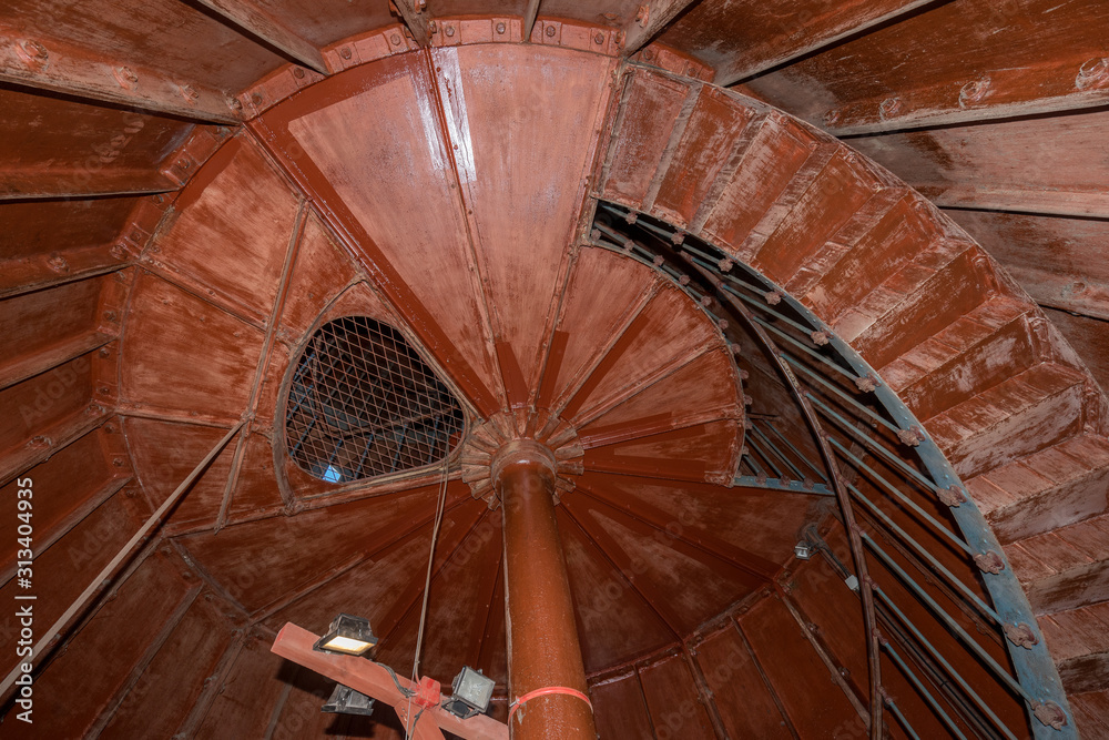Old lighthouse on the inside. Red iron spiral stairs, round window and ...