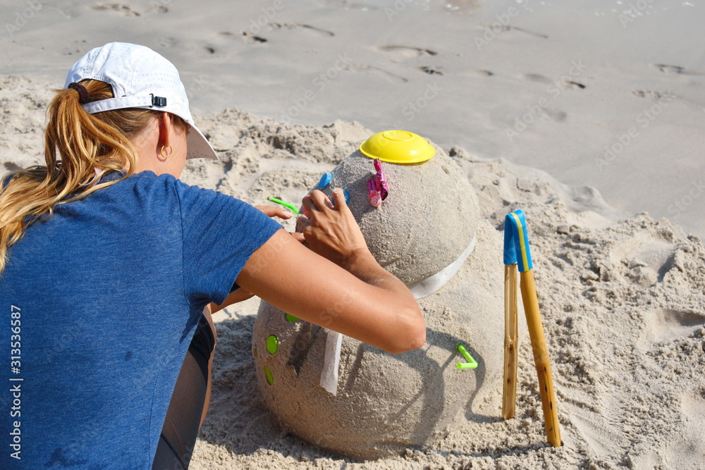 Girl makes a Sandman on the beach. Woman builds a snowman on the beach ...