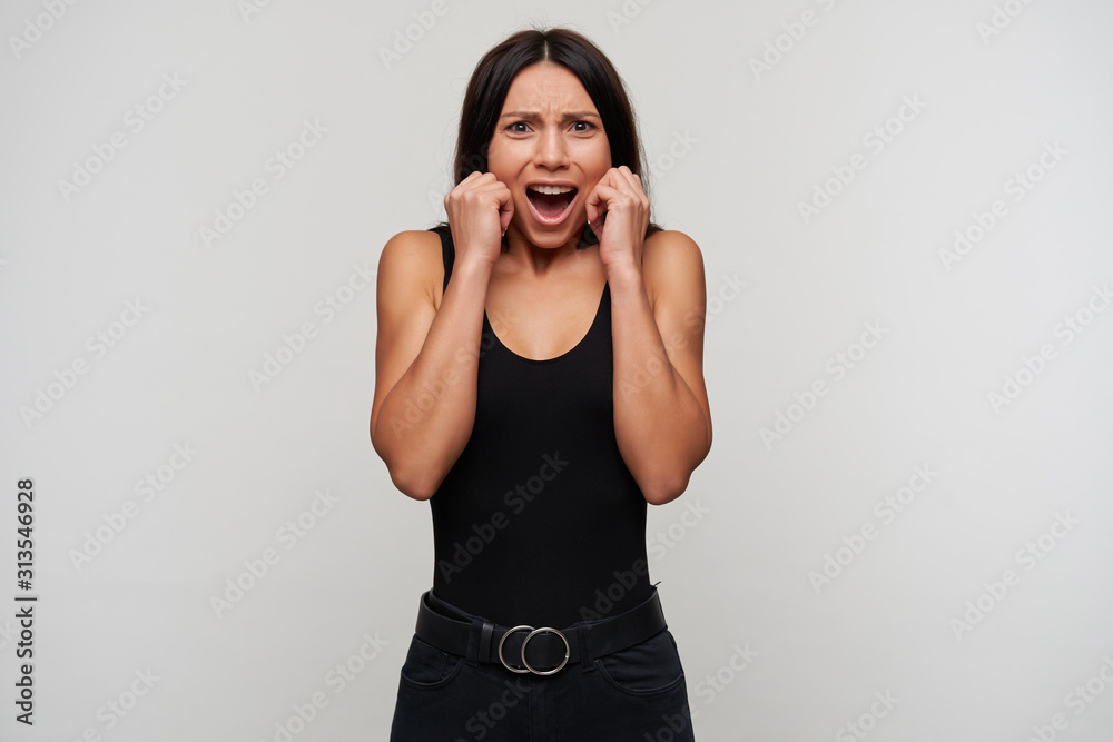Frightened young dark haired woman with casual makeup raising hands to ...