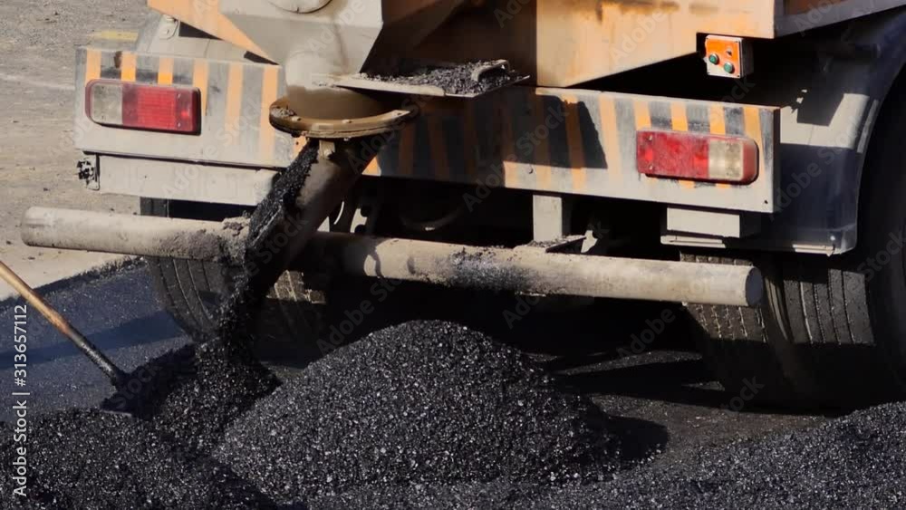 Truck dumping hot asphalt on the road. Large industrial machine pour ...