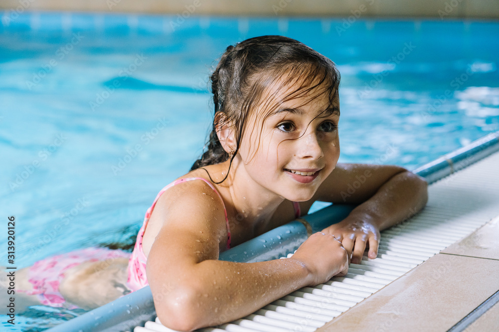 Portrait little girl having fun in indoor swimming-pool. The girl is ...
