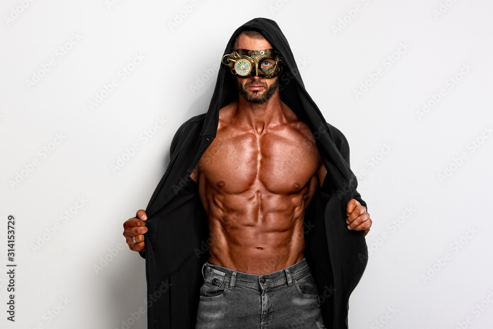 Handsome masked macho man posing in unbuttoned coat with hood exposing ...