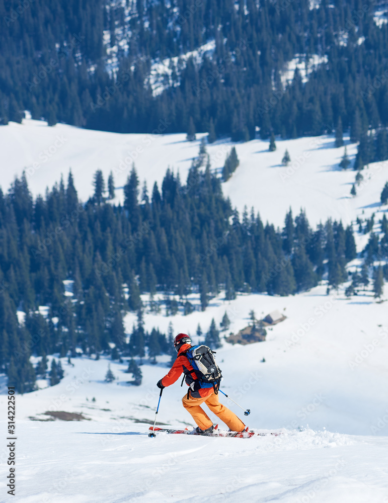 Back view of skier going down the slope at a ski resort with ...