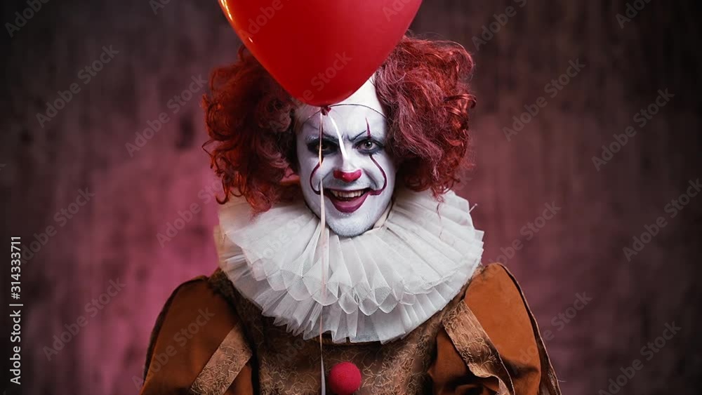 Creepy clown releases a red ball and shows his face. Clown in a ...