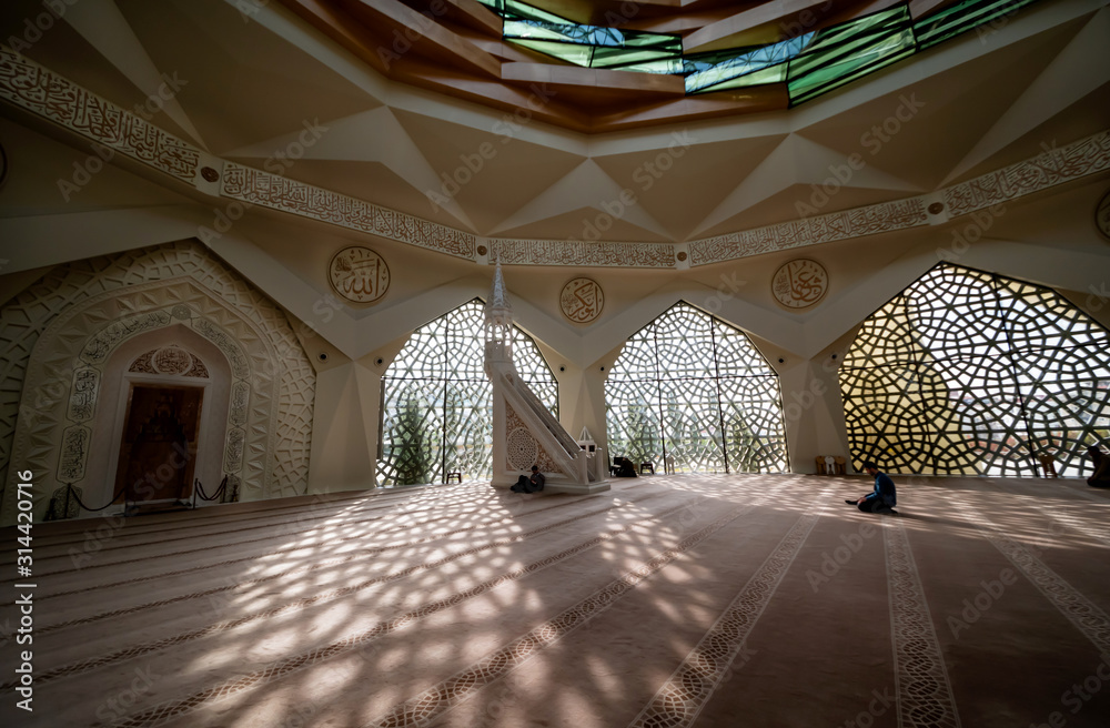 Local people praying inside the modern mosque. Sunlight shines through ...
