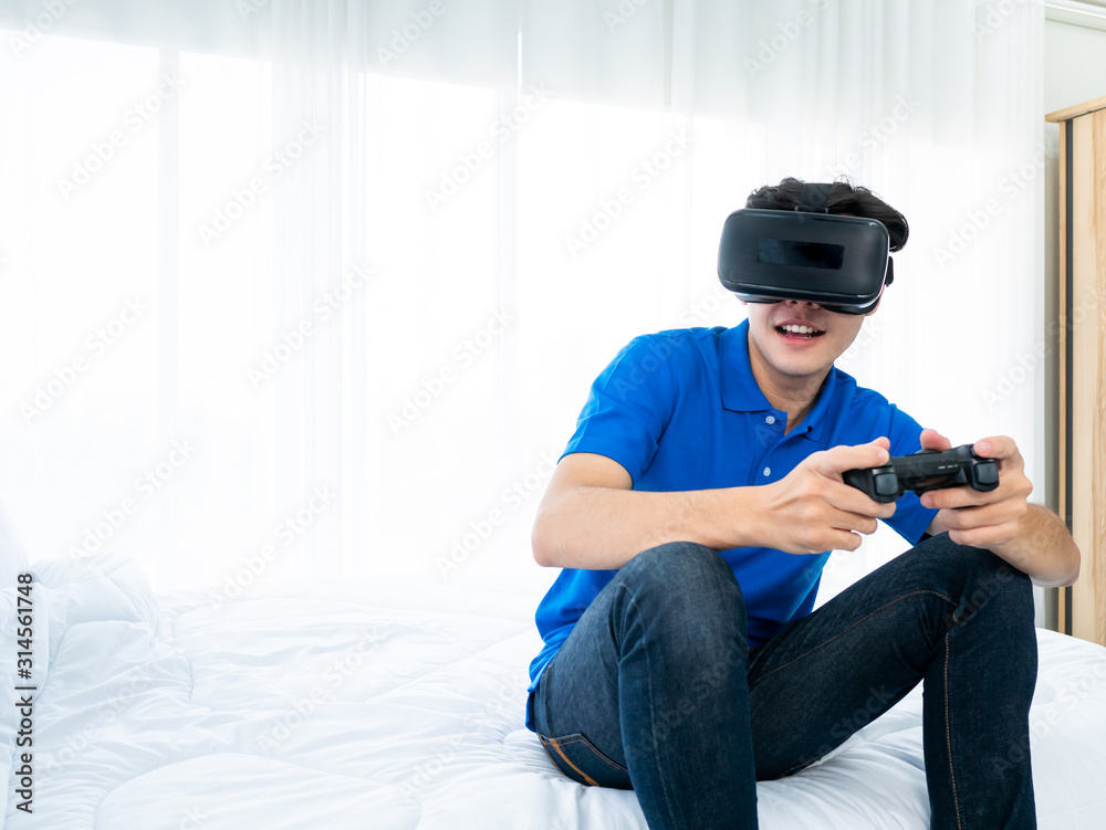 Asian young man sitting and enjoy playing game with VR or virtual ...