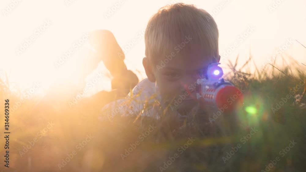boy shoots from toy weapons gun. little boy plays war lies on the ...