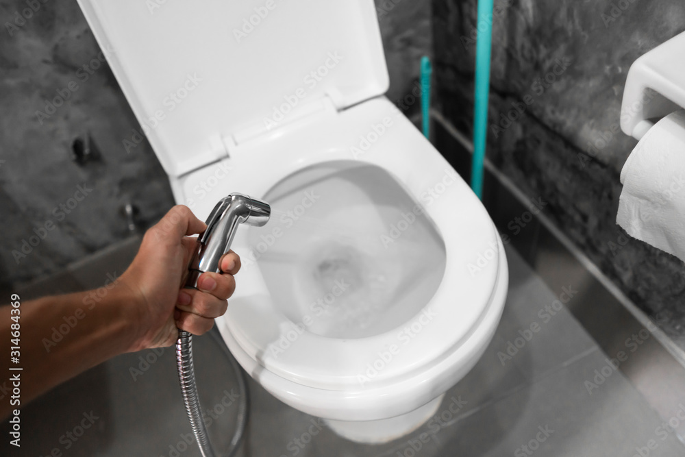Using of bidet shower with a white toilet. Bidet shower in male hand ...