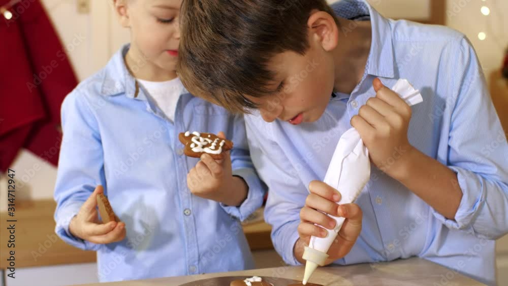 Two brothers is decorating a Christmas cookies with pastry bag at home ...