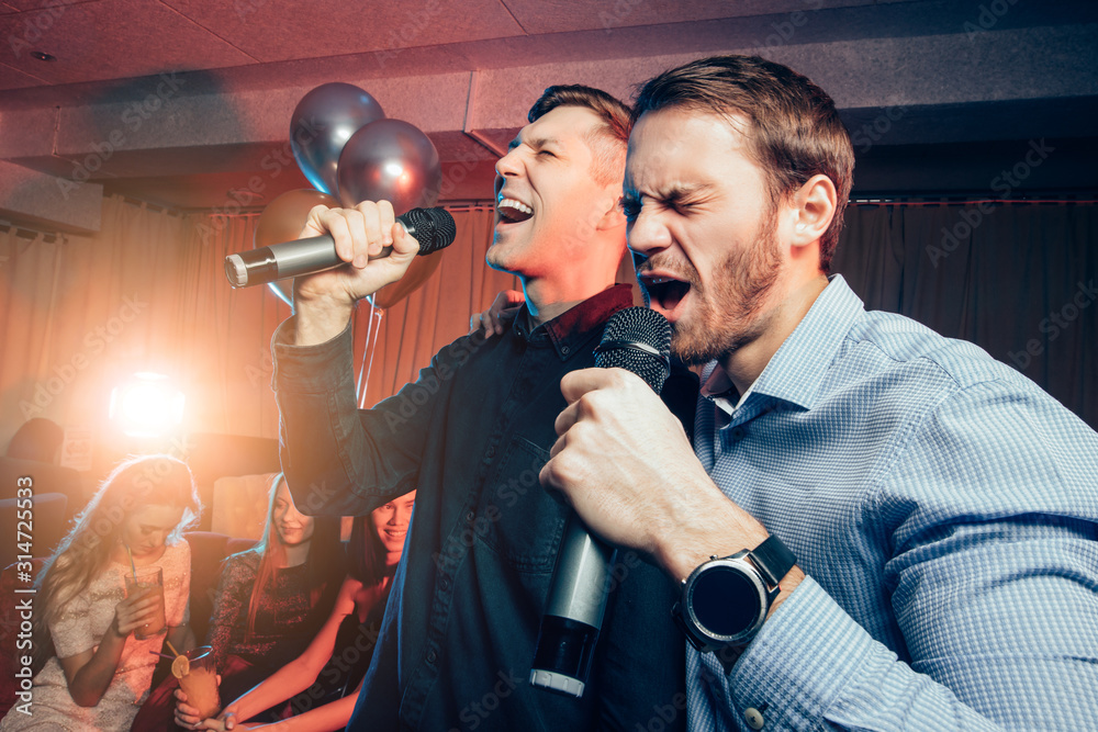 two young caucasian men in t-shirts singing in microphone in karaoke ...