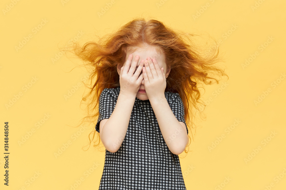 Isolated shot of timid little girl being shy, covering eyes. Red haired ...