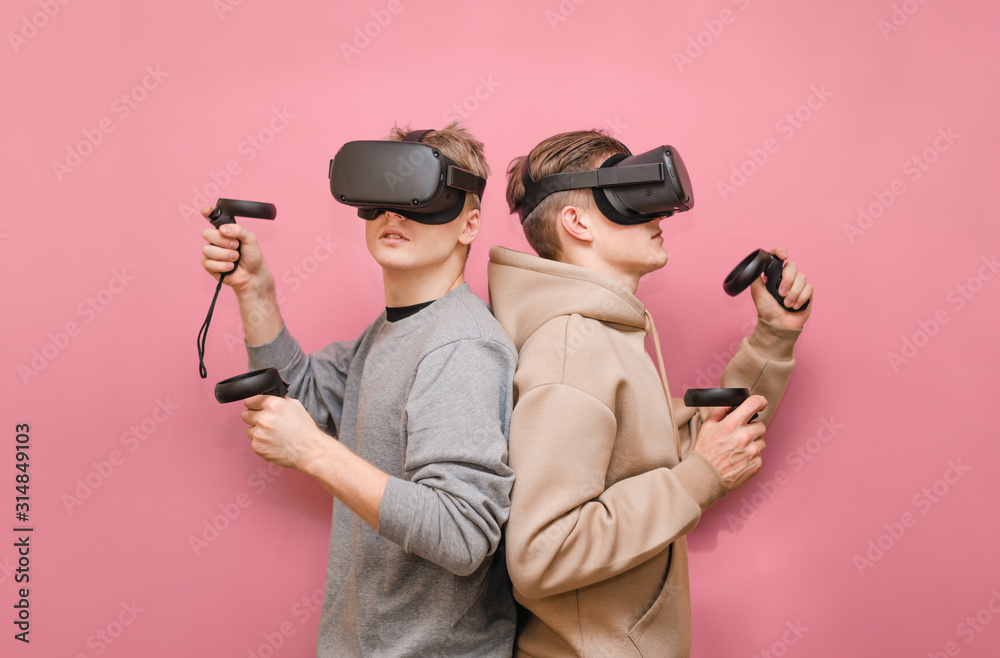 Two young men in VR helmets on their heads stand side by side on a pink ...