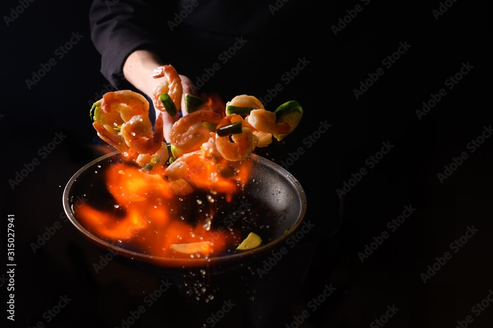 Professional cook cooks shrimps with vegetables on fire. Cooking ...