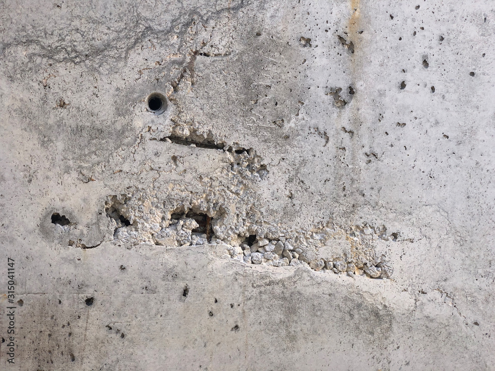 Concrete surface with caverns and exposed gravel stones and ...