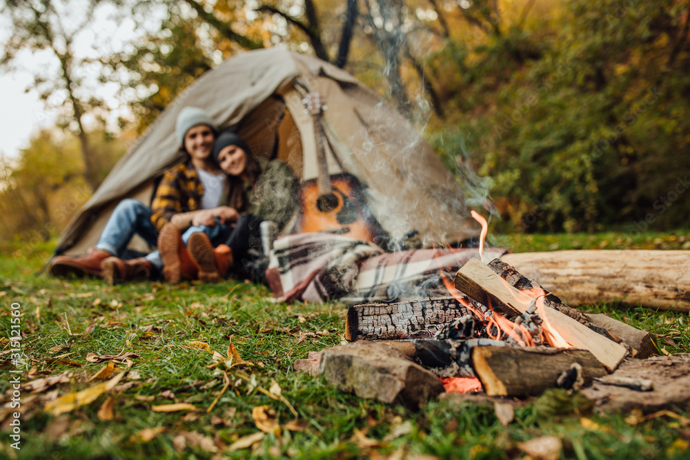 Focus on fire near tent. Young loved couple of tourists have a date in ...