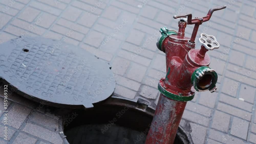 Close-up fire hydrant connected to an open hatch in the city. Old red ...
