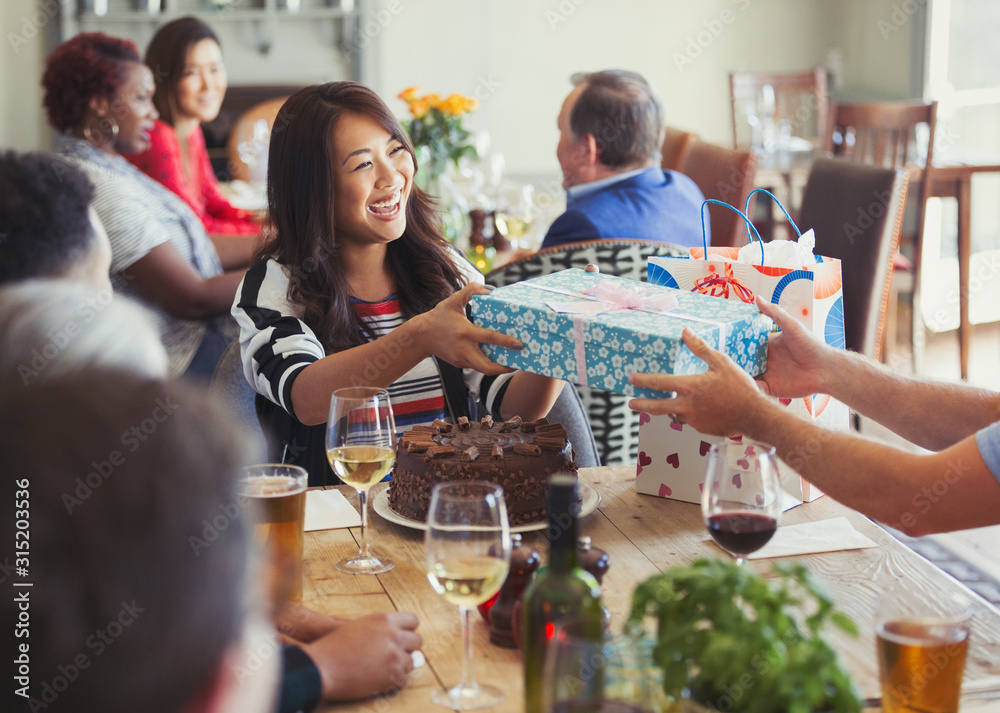 Smiling woman receiving birthday gift from friend at restaurant table ...