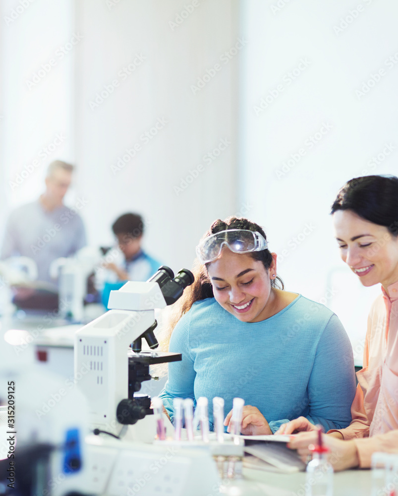 Smiling female science teacher and girl student reading textbook at ...