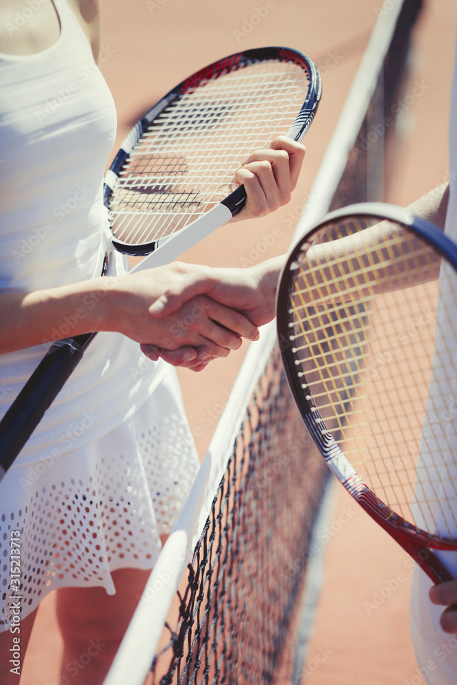 Tennis players handshaking in sportsmanship at net on sunny tennis ...