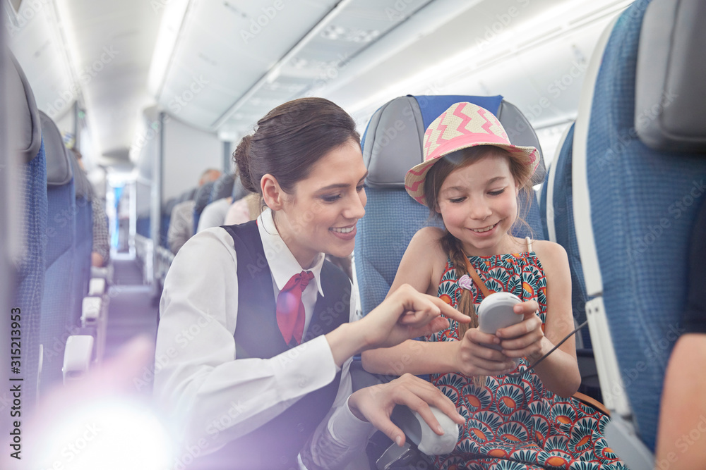 Flight attendant helping girl passenger remote control on airplane ...