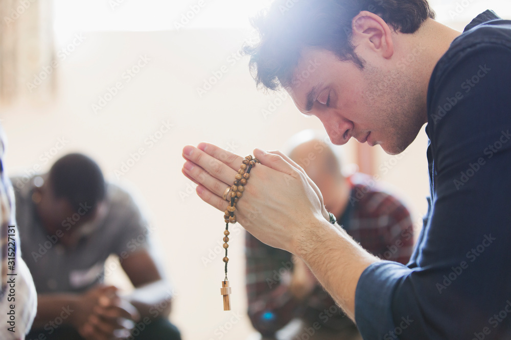 Serene man praying with rosary in prayer group Stock Photo | Adobe Stock