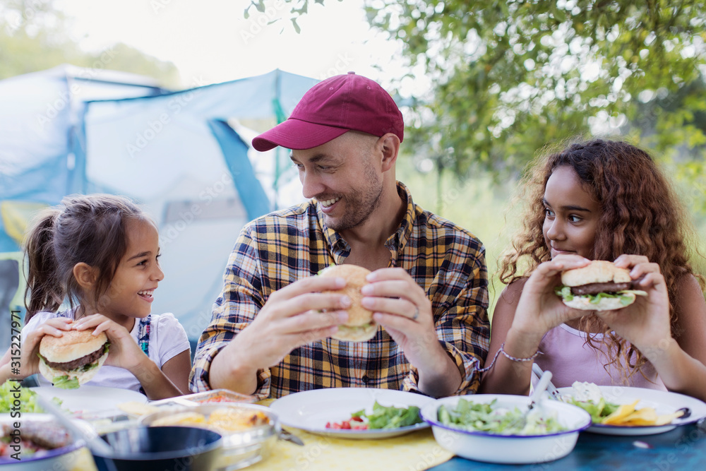 Father and daughters enjoying barbecue hamburger lunch at campsite ...