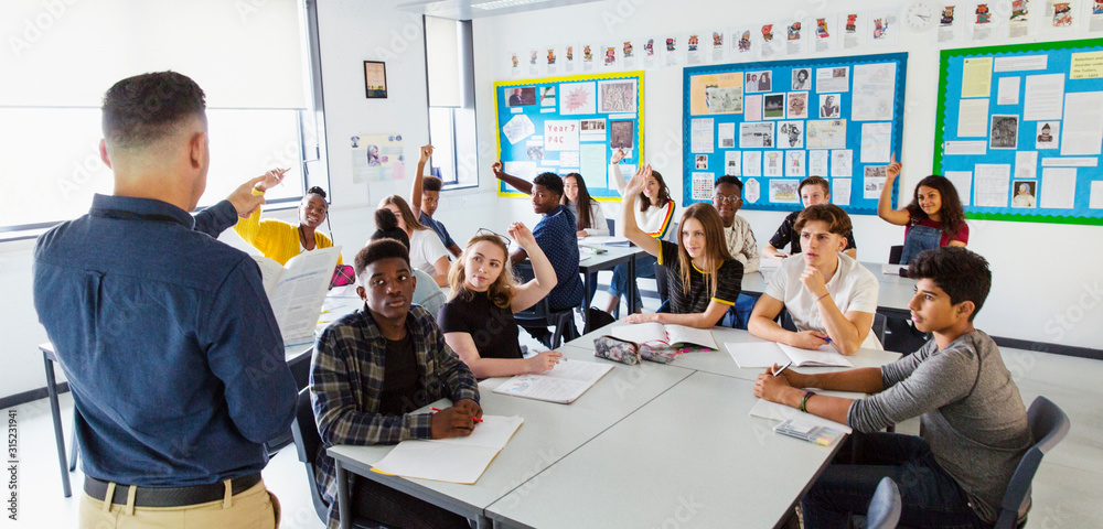 High school teacher calling on students with hands raised in classroom ...