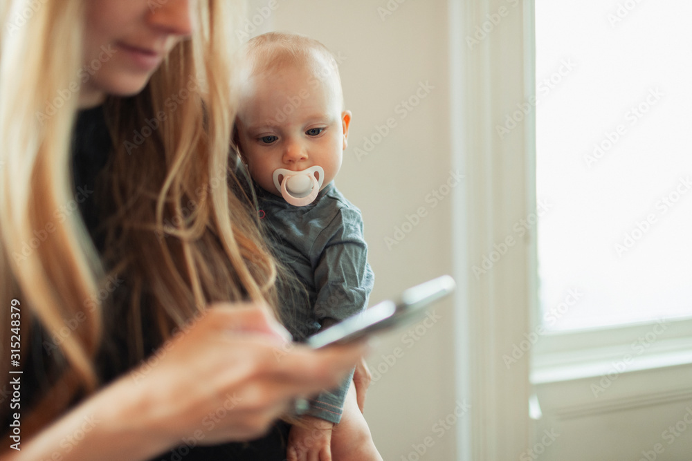 Curious baby girl with pacifier watching mother using smart phone Stock ...