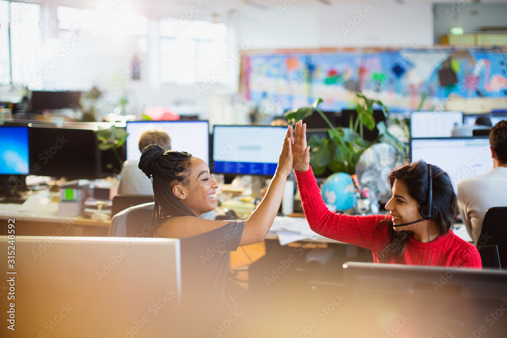 Happy businesswomen high-fiving at computers in open plan office Stock ...