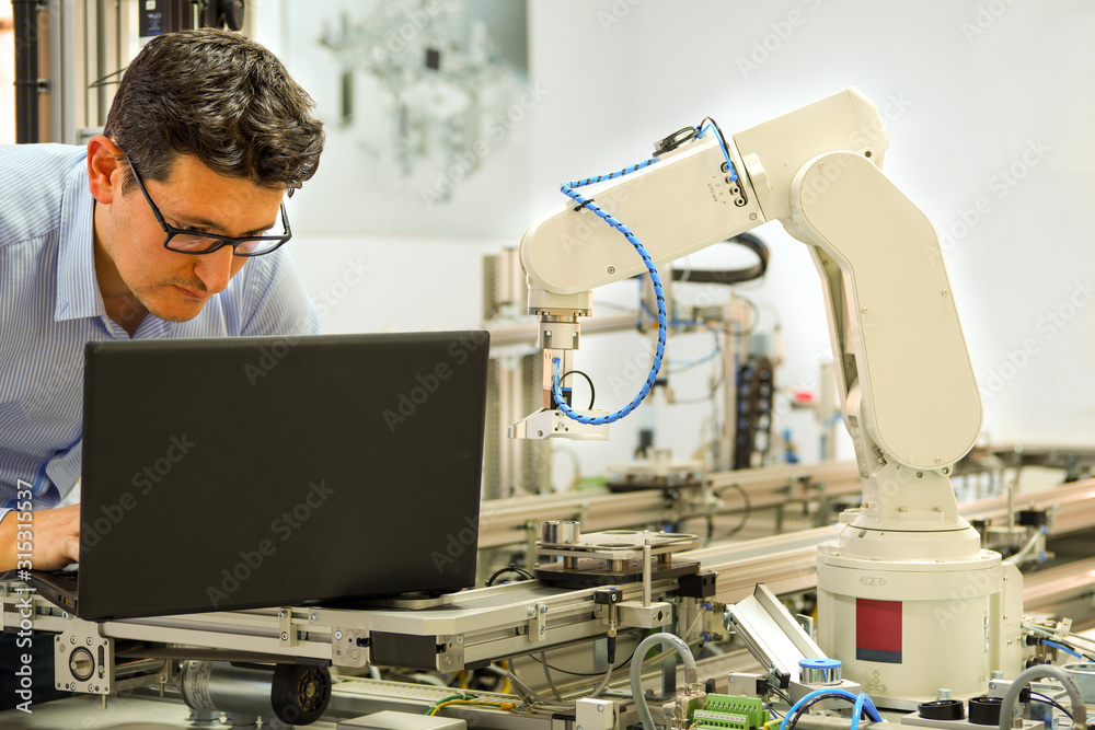 Close-up robot arm. Engineer is working on laptop to programming smart ...