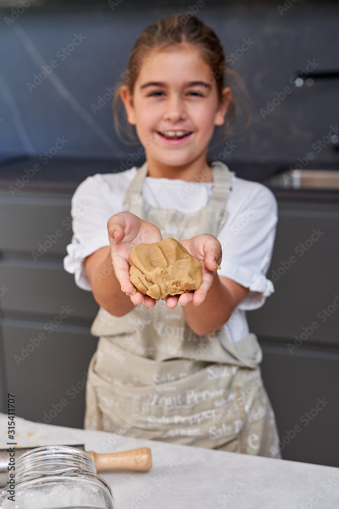 Content girl in blue back splash crumpling brown paste above table with ...