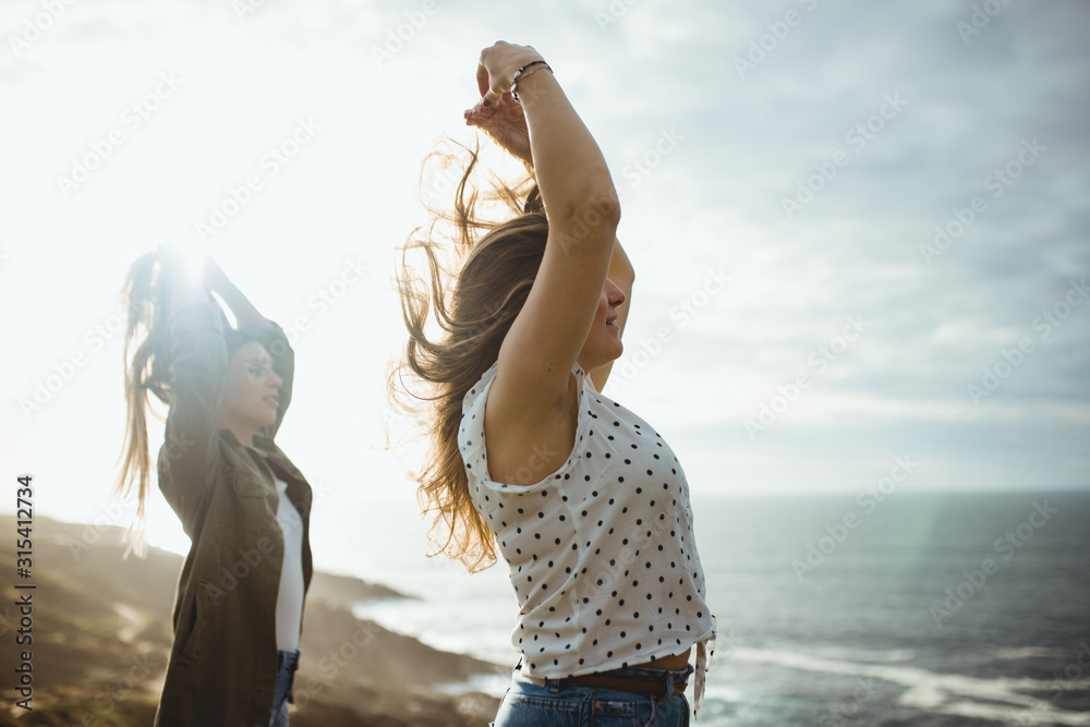 Side view of young women in back lit raising hands and holding hair ...
