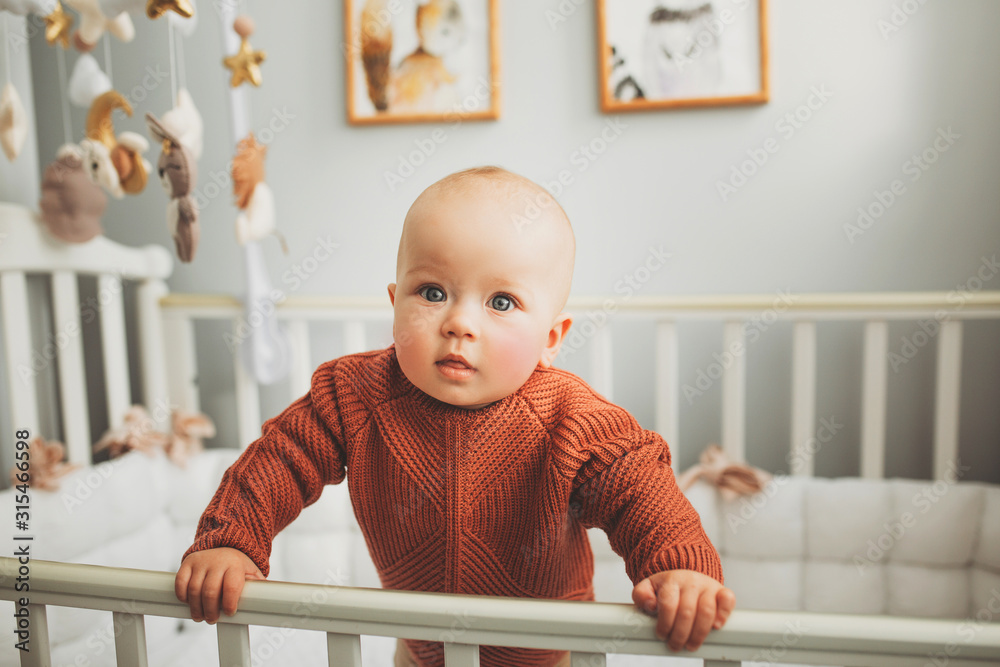 Beautiful little girl in a crib in a cozy light room in a sweater of ...