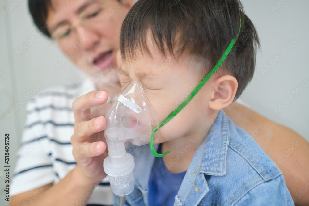 Asian father helping his toddler son with inhalation therapy by the ...