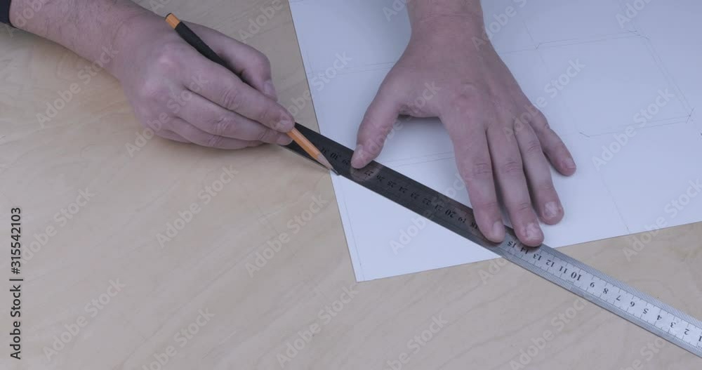 Male hand drawing a line with a pencil and a metal ruler on the sheet ...